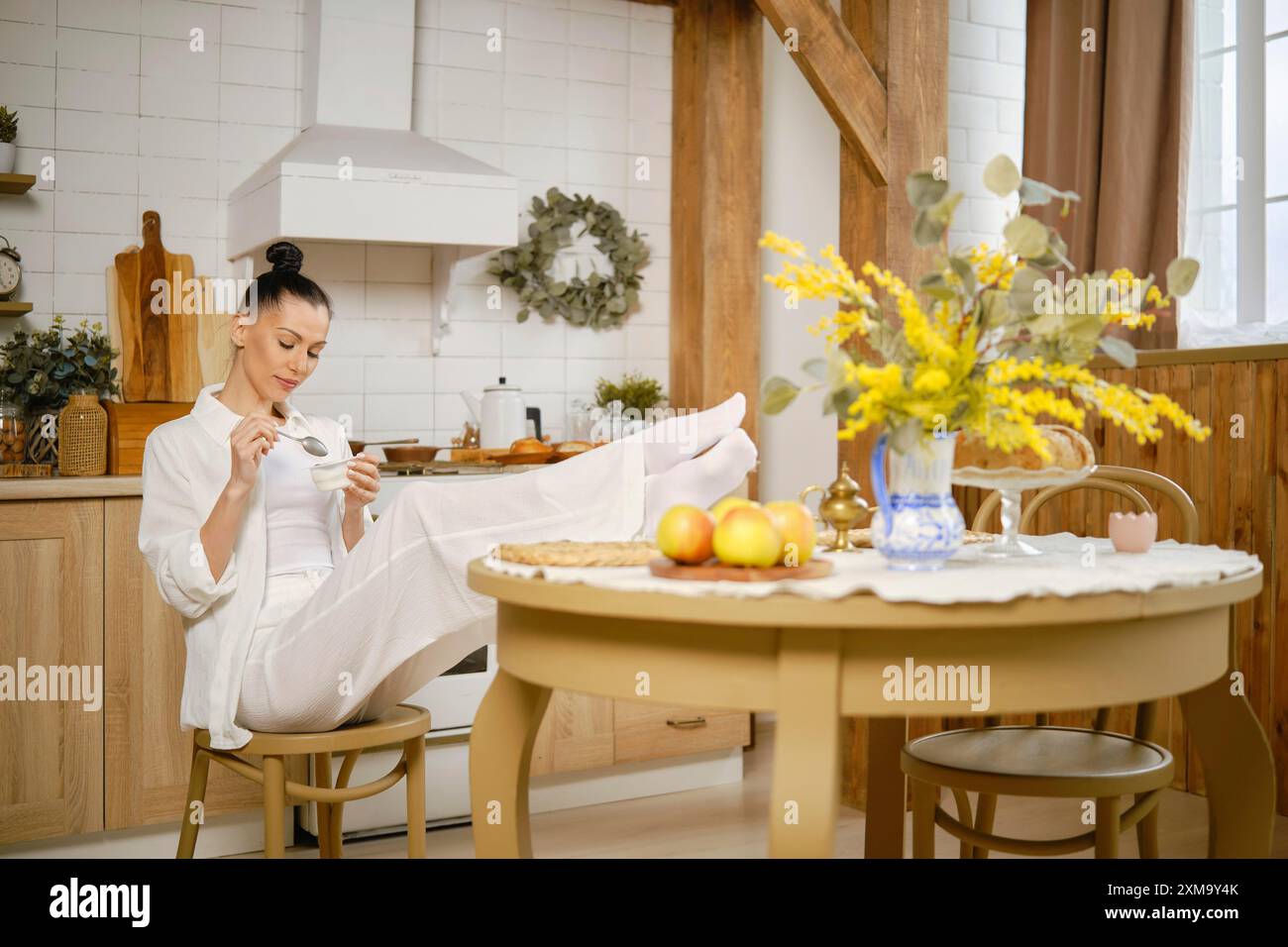 A woman in cotton outfit sits in the kitchen with her feet on the table ...