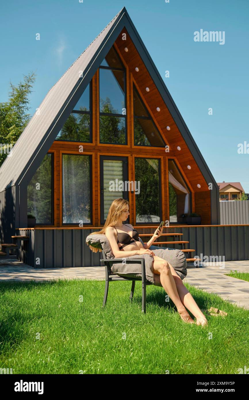 Slender woman lounging in a chair, enjoying the sun with a smartphone ...