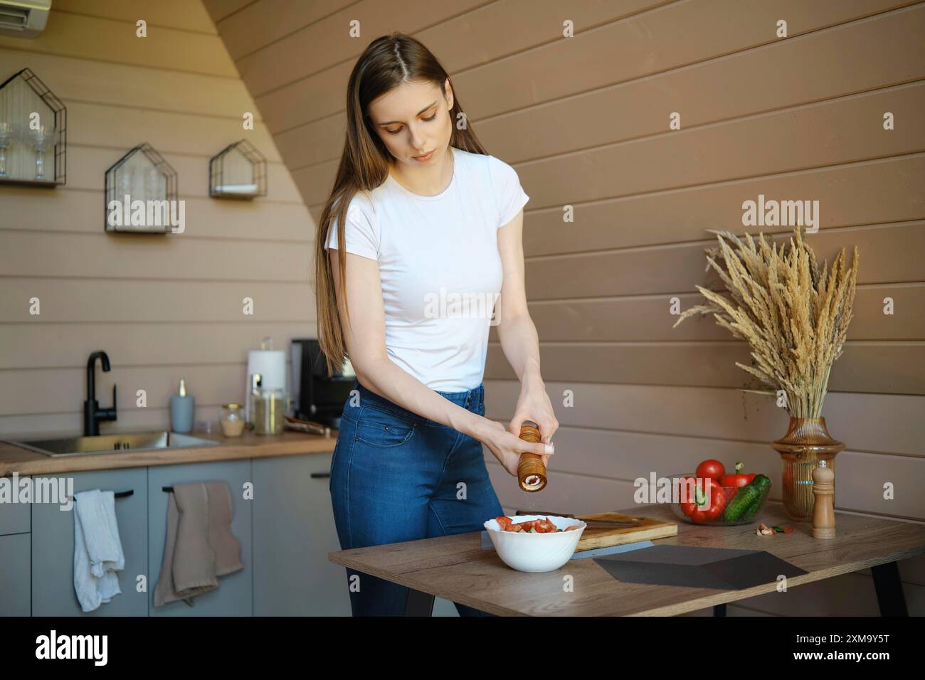 Woman adding pepper in cucumber and tomato vegetable salad, cooking in ...