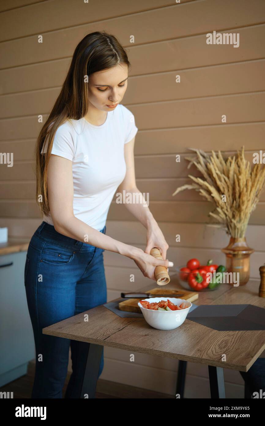 Woman adding sea salt from a hand mill to a bowl with vegetable salad ...