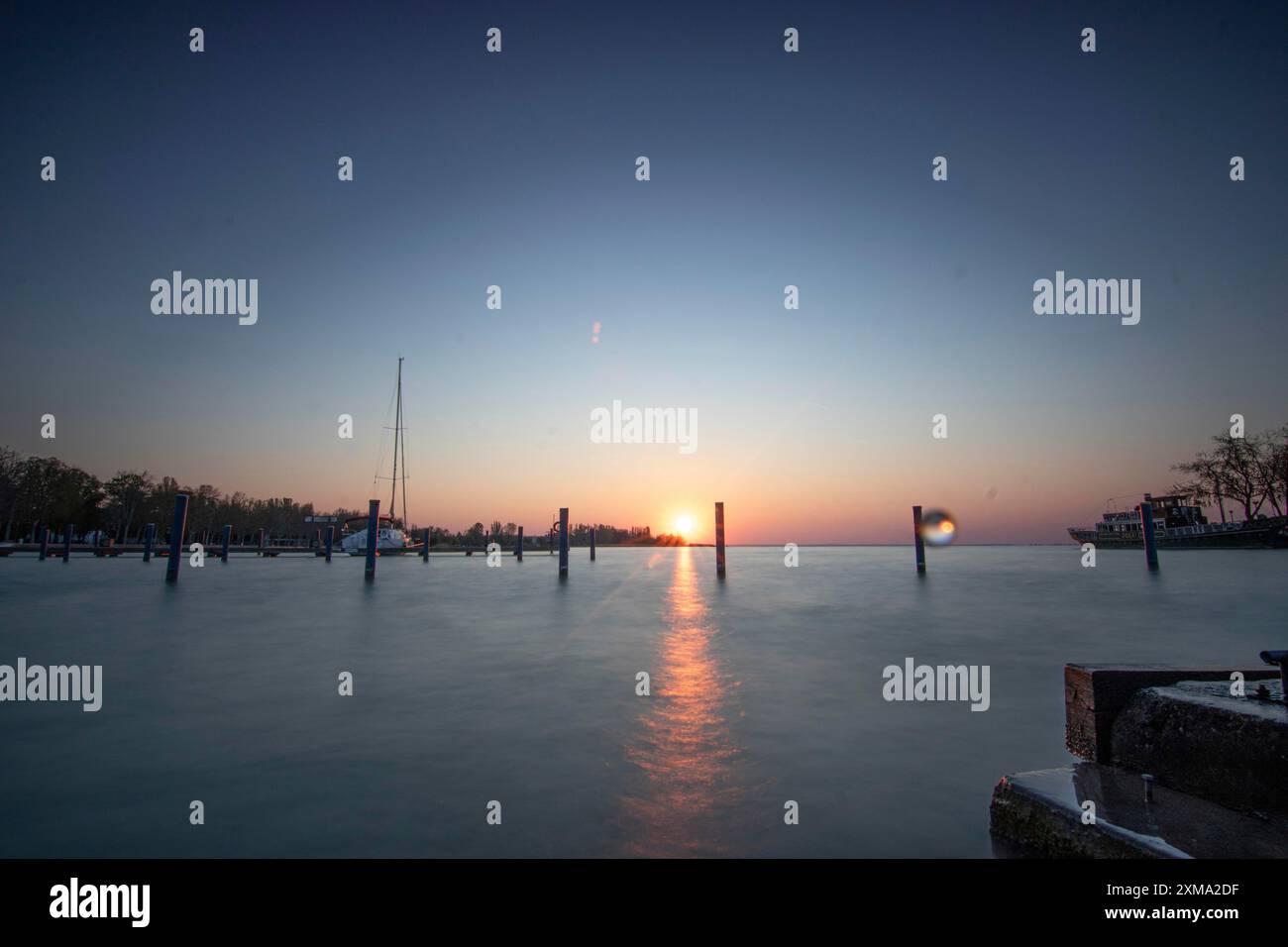 Sunrise on the shore and harbour of a lake in summer. Colourful sky ...