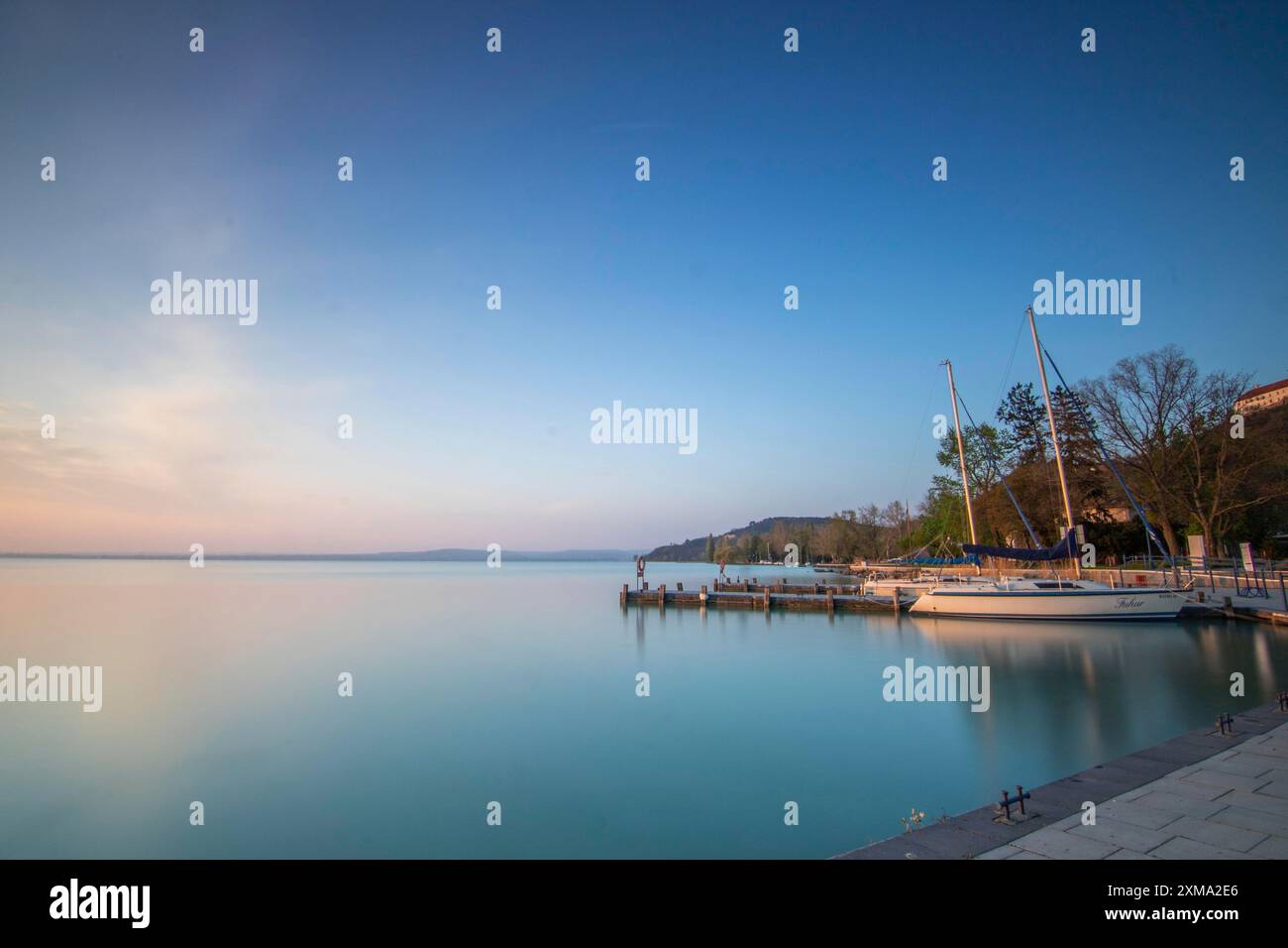 Sunrise on the shore and harbour of a lake in summer. Colourful sky ...