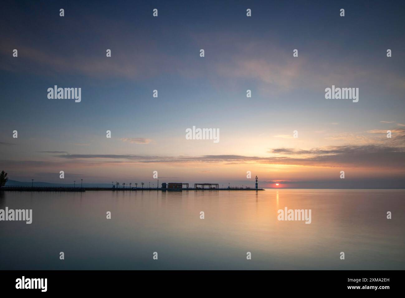 Sunrise on the shore and harbour of a lake in summer. Colourful sky ...