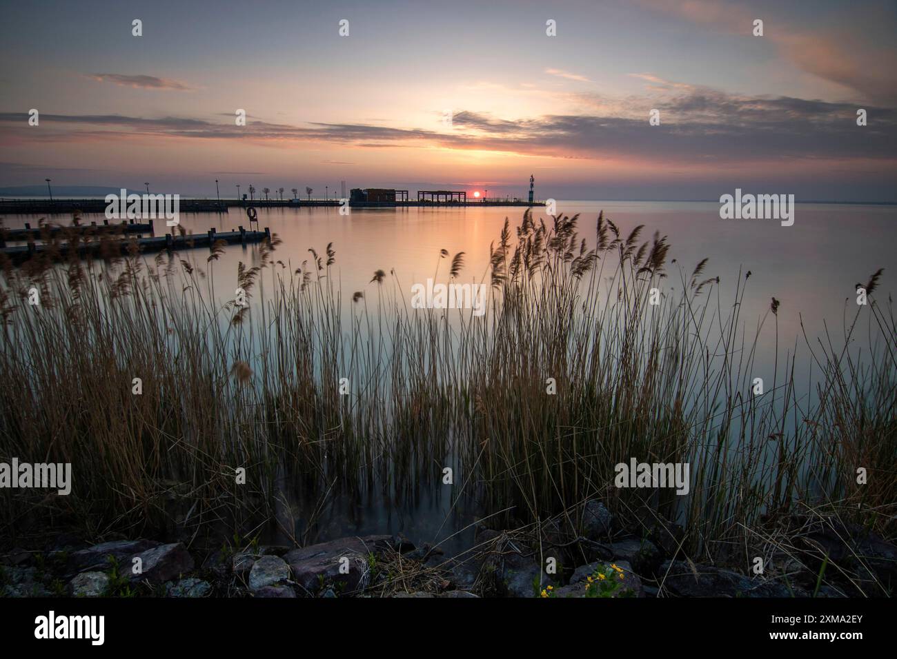 Sunrise on the shore and harbour of a lake in summer. Colourful sky ...