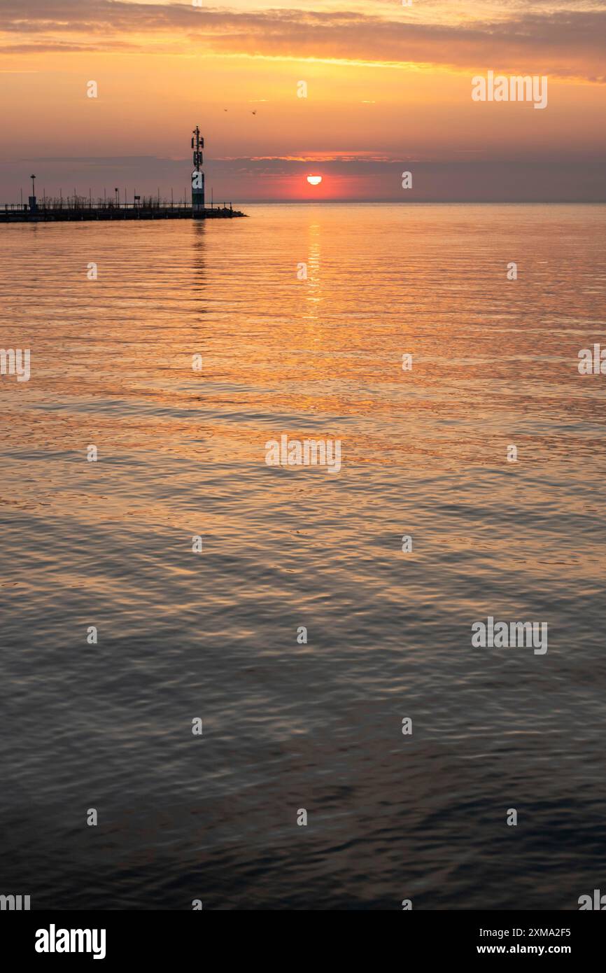 Sunrise on the shore and harbour of a lake in summer. Colourful sky ...