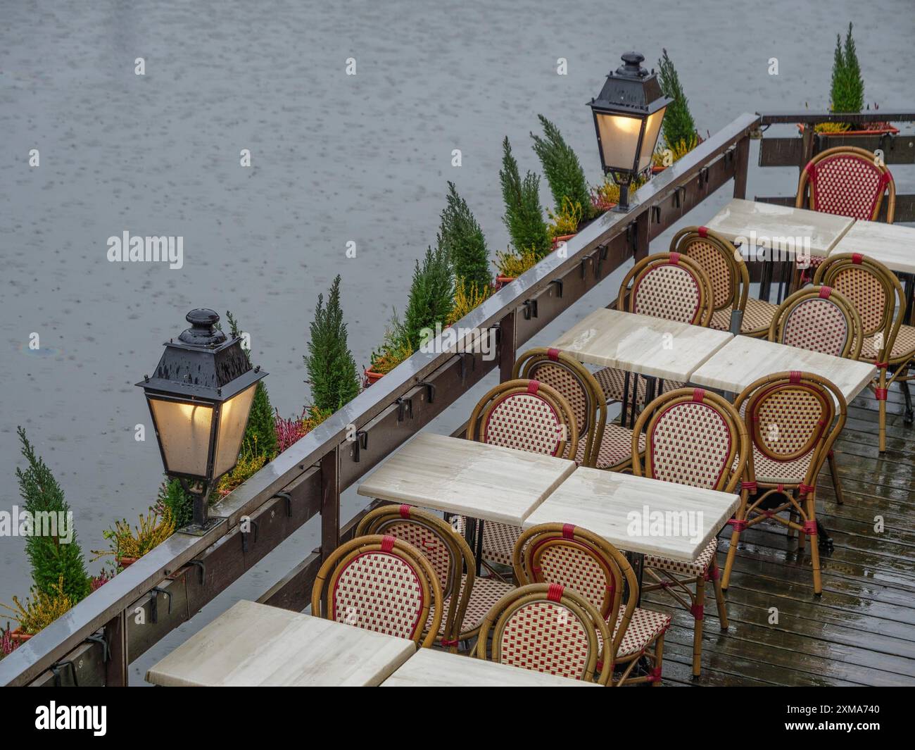 Empty outdoor terrace of a cafe with chairs and tables, rain-swept and ...