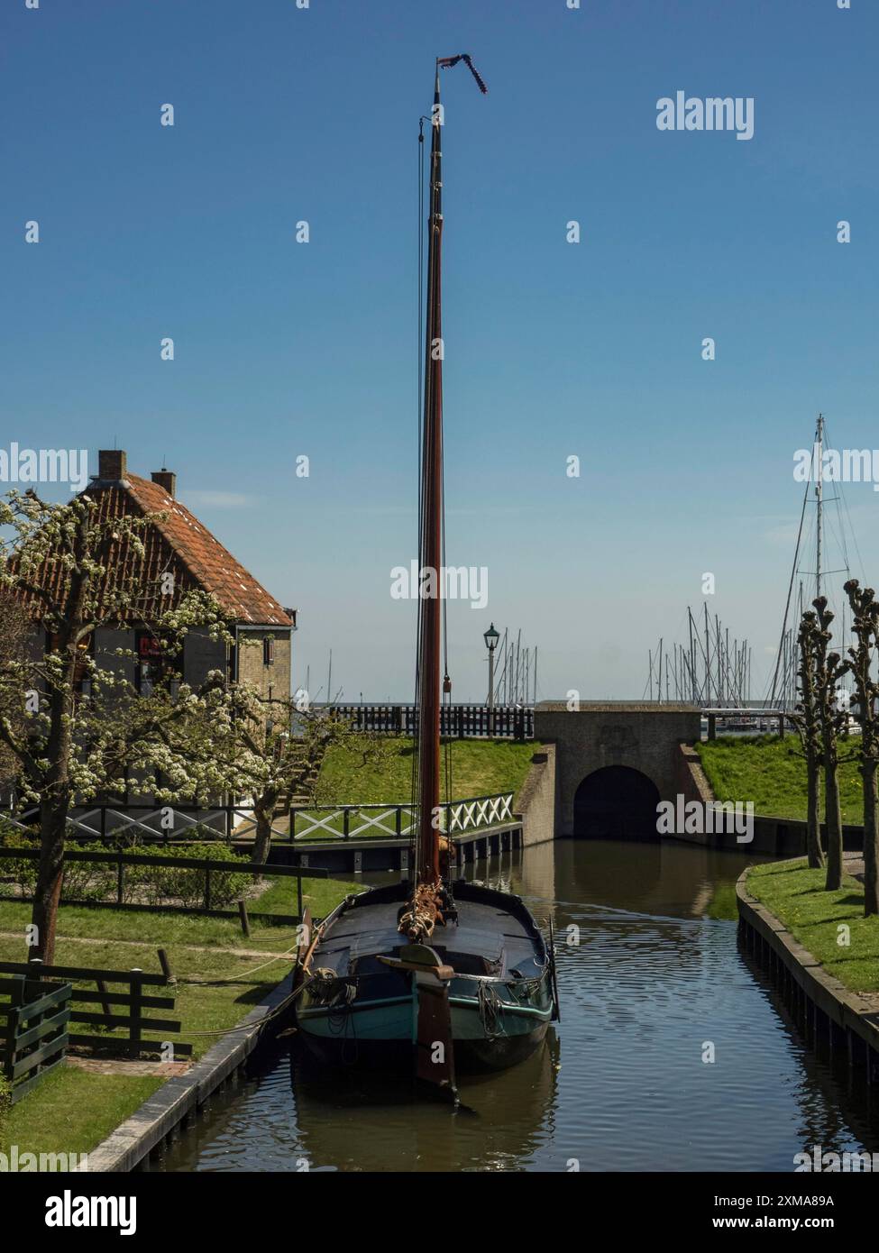 Simple sailing boat along a quiet canal in front of a traditional house ...