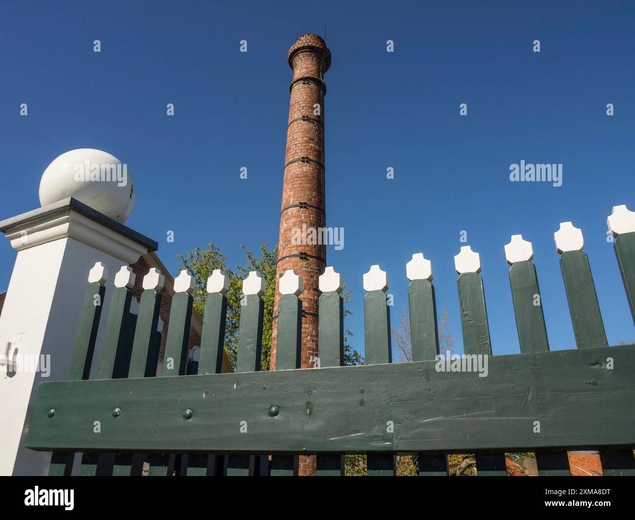 Brick chimney behind a green fence in front of a clear blue sky ...
