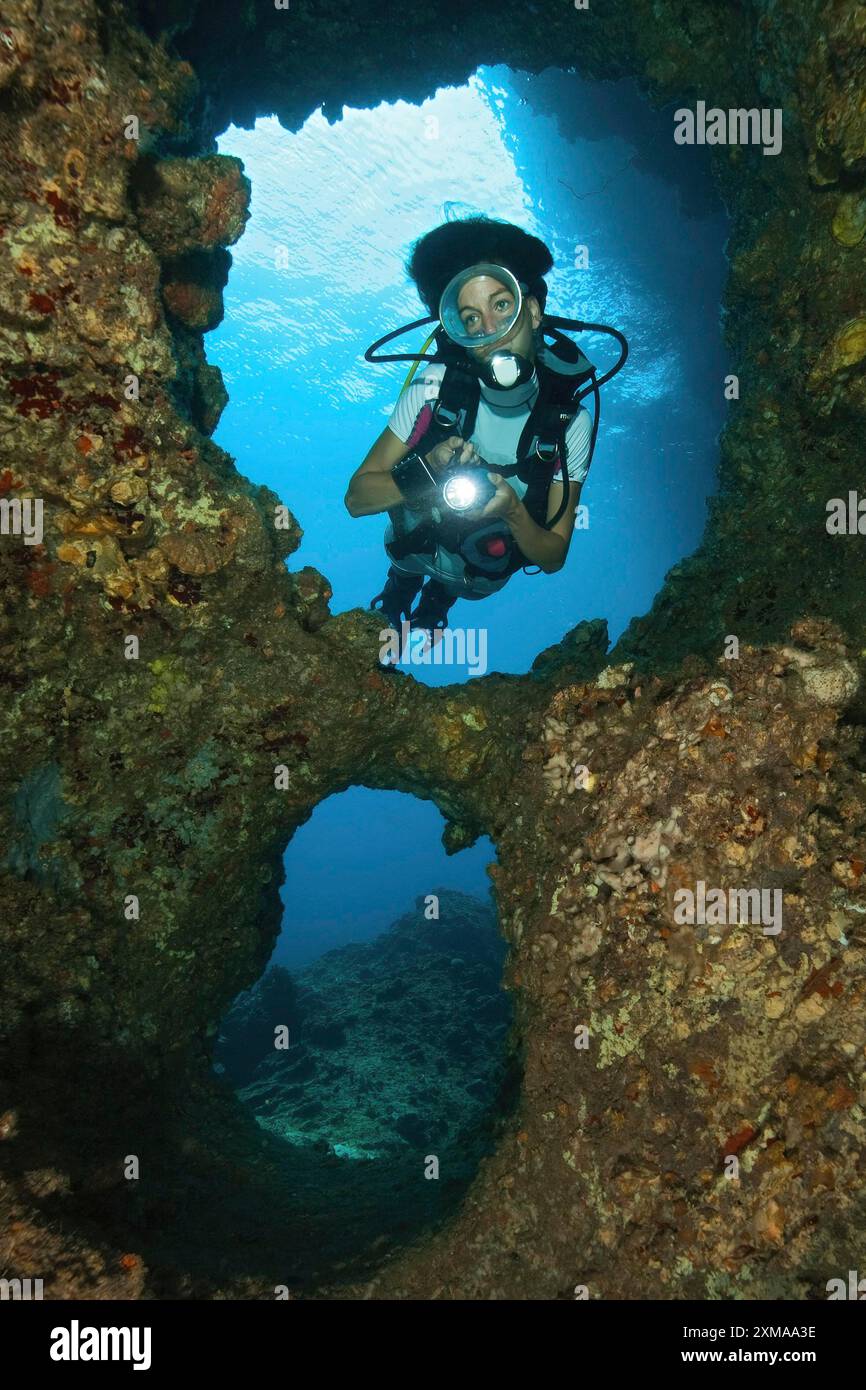 Female diver diving in underwater cave in coral reef looking through ...