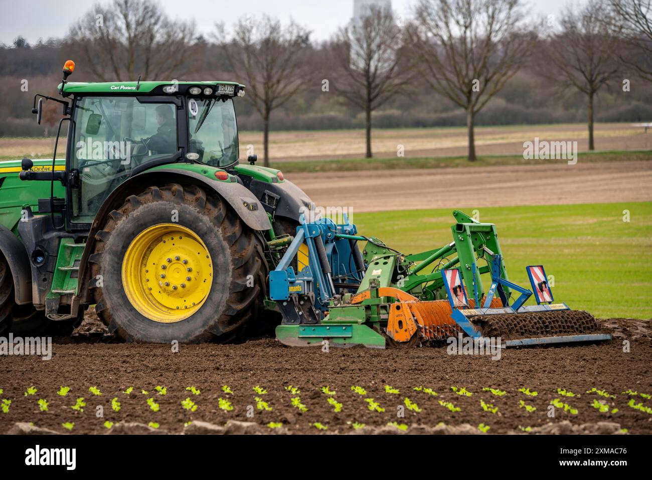 Tractor with a power harrow prepares the soil of a field for planting ...