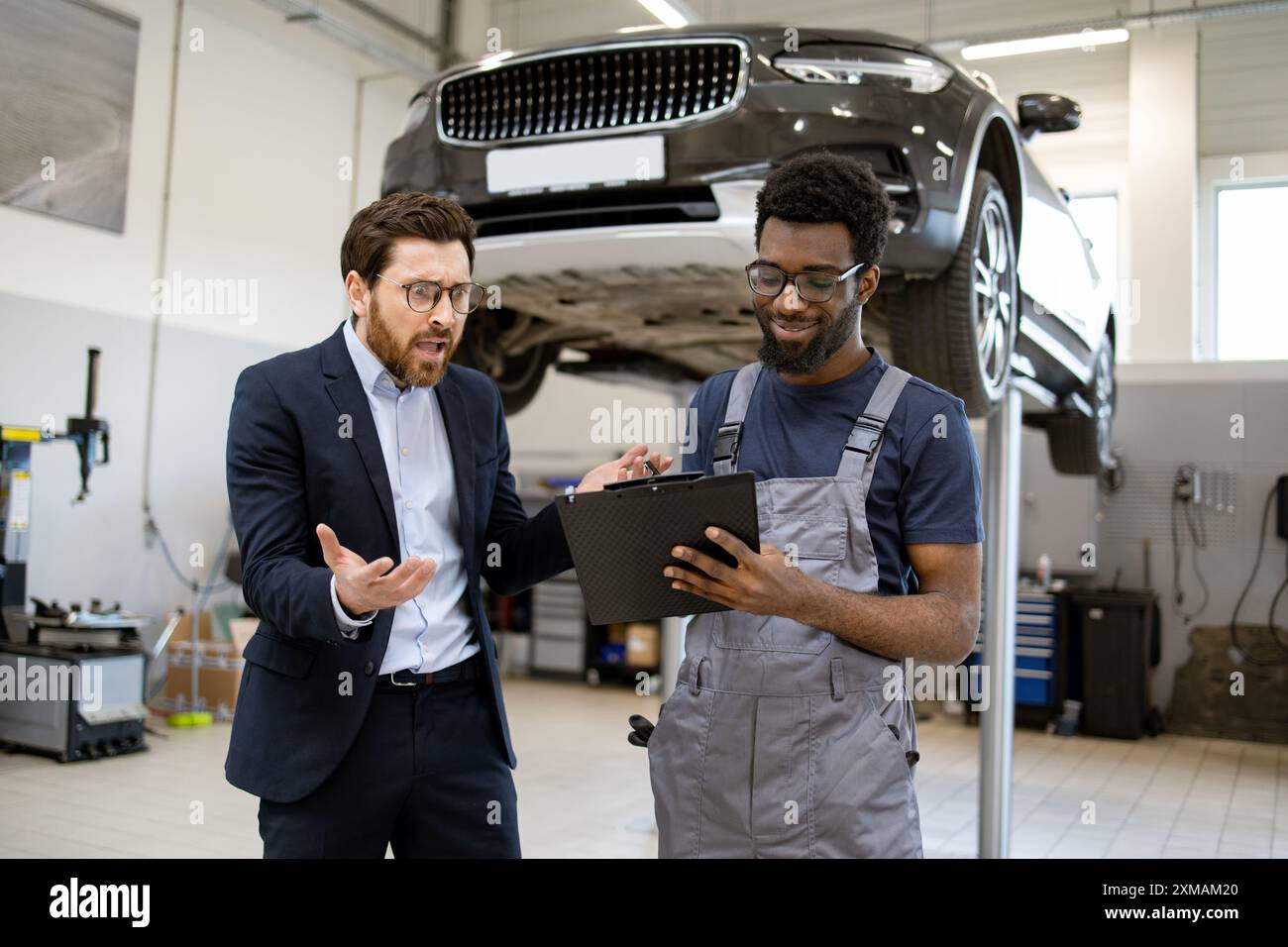 Mechanic discussing car issues with businessman inside auto repair shop ...