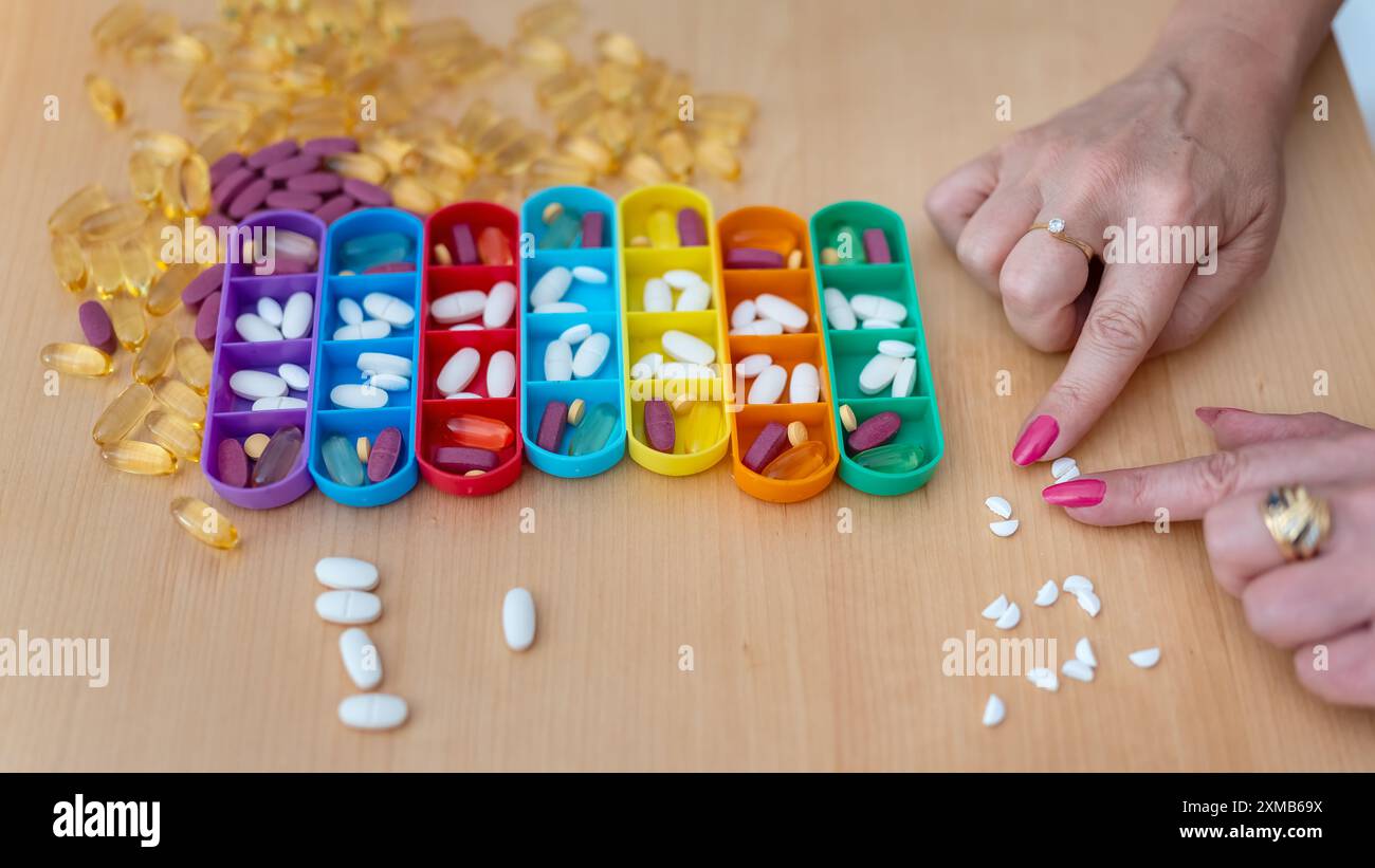 Mature woman splits a white pill in half with her fingers to organize ...
