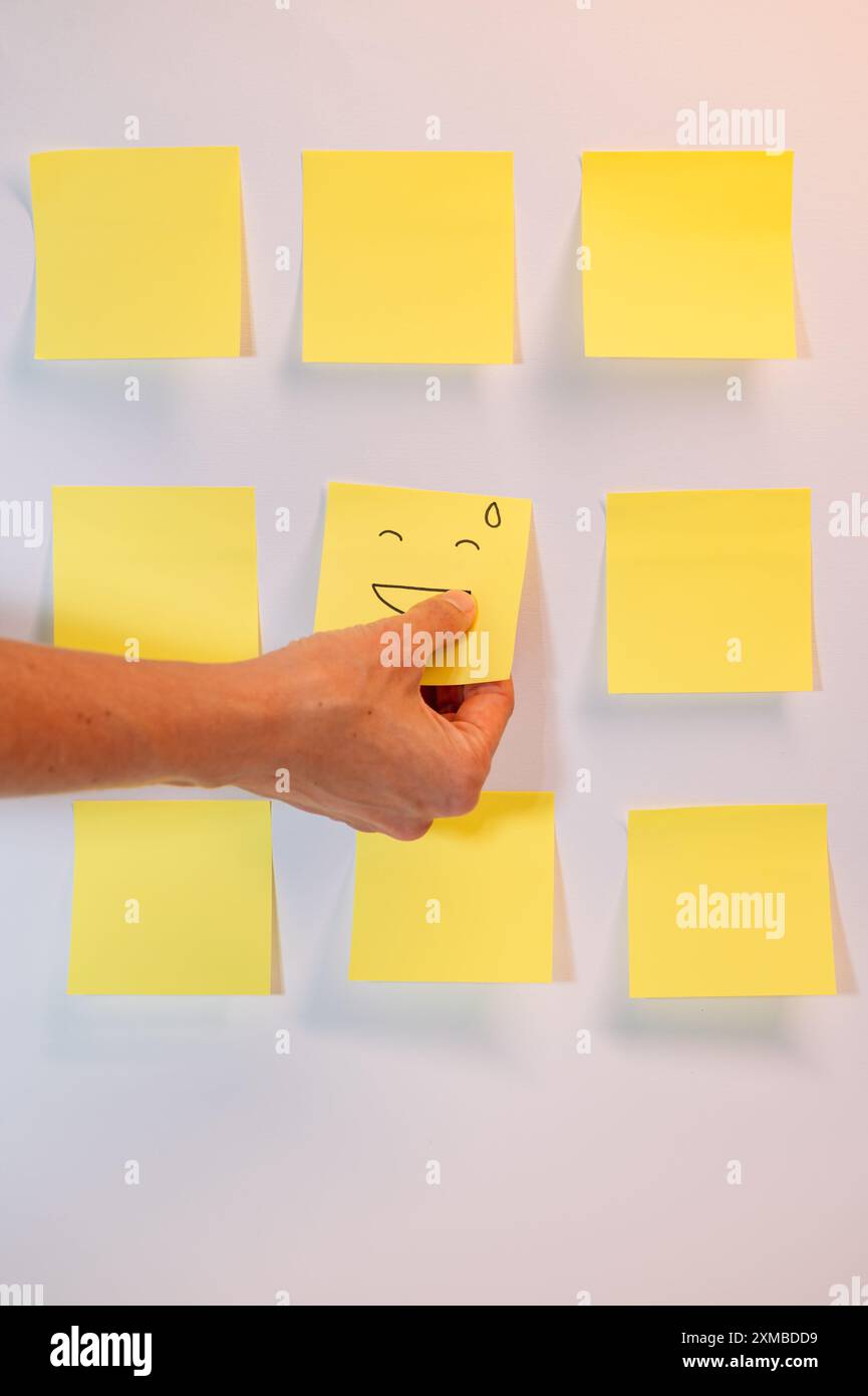 A hand is holding a yellow sticky note with a smiley face on it. The ...