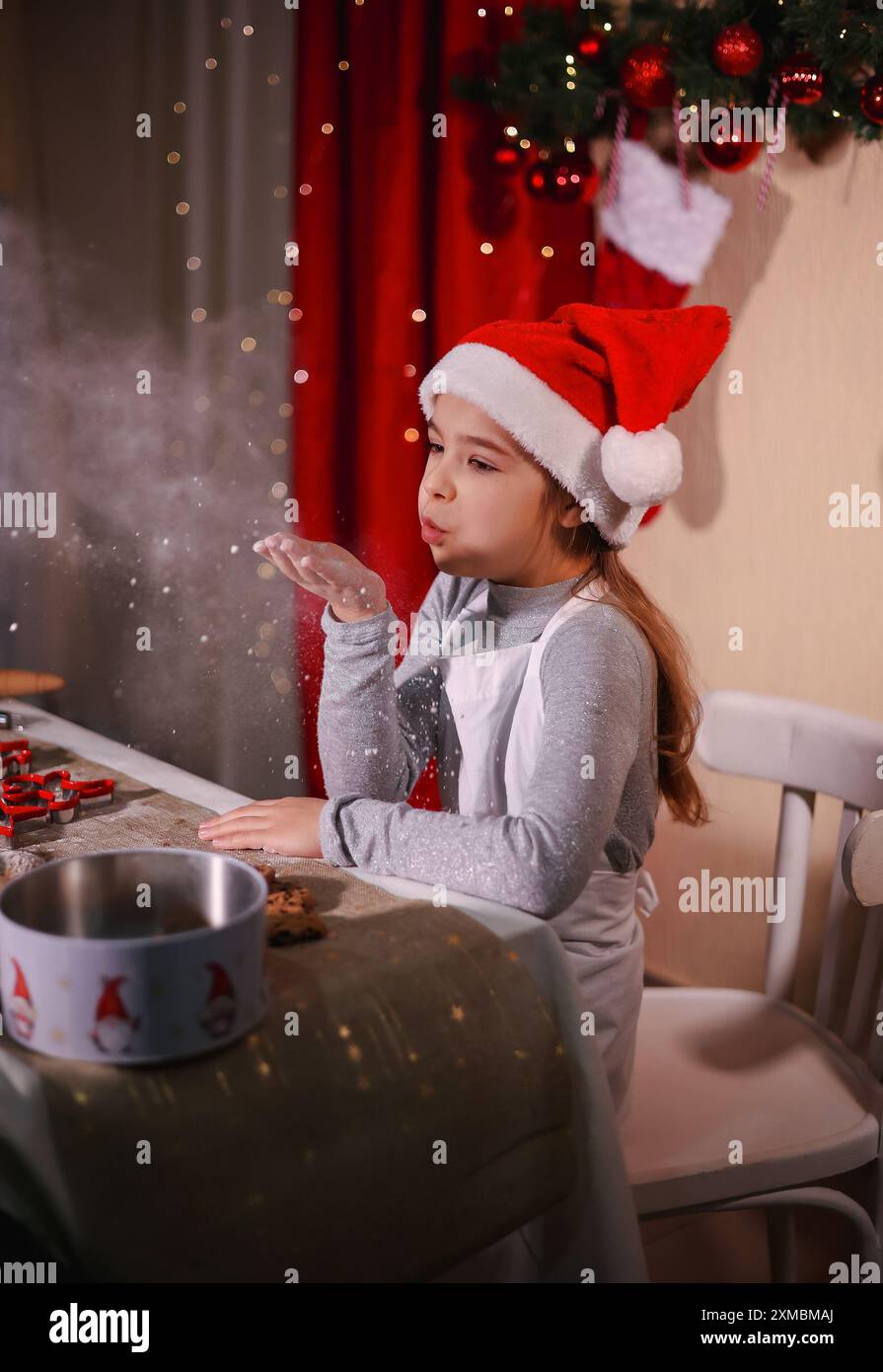 A girl in a Santa hat blows magic dust from her palm against the ...