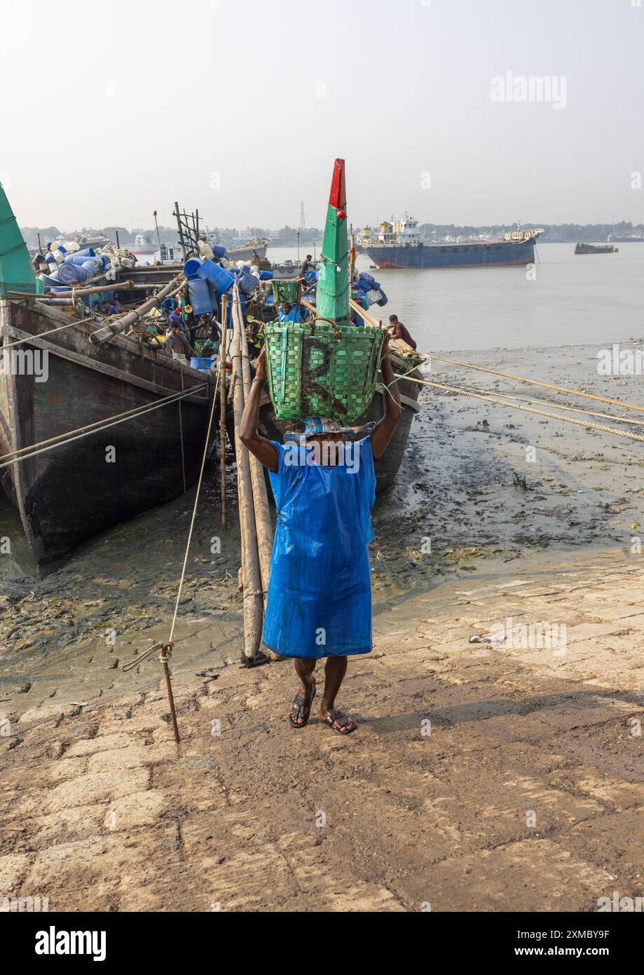 A bangladeshi porter carries a load from a trawler at the morning fish market, Chittagong ...