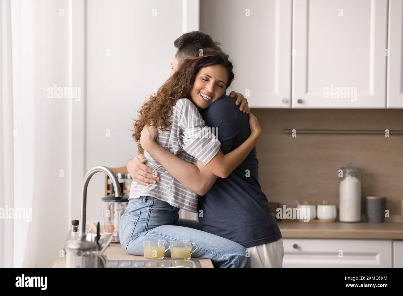 Pretty enamored woman sitting on kitchen countertop and cuddling ...