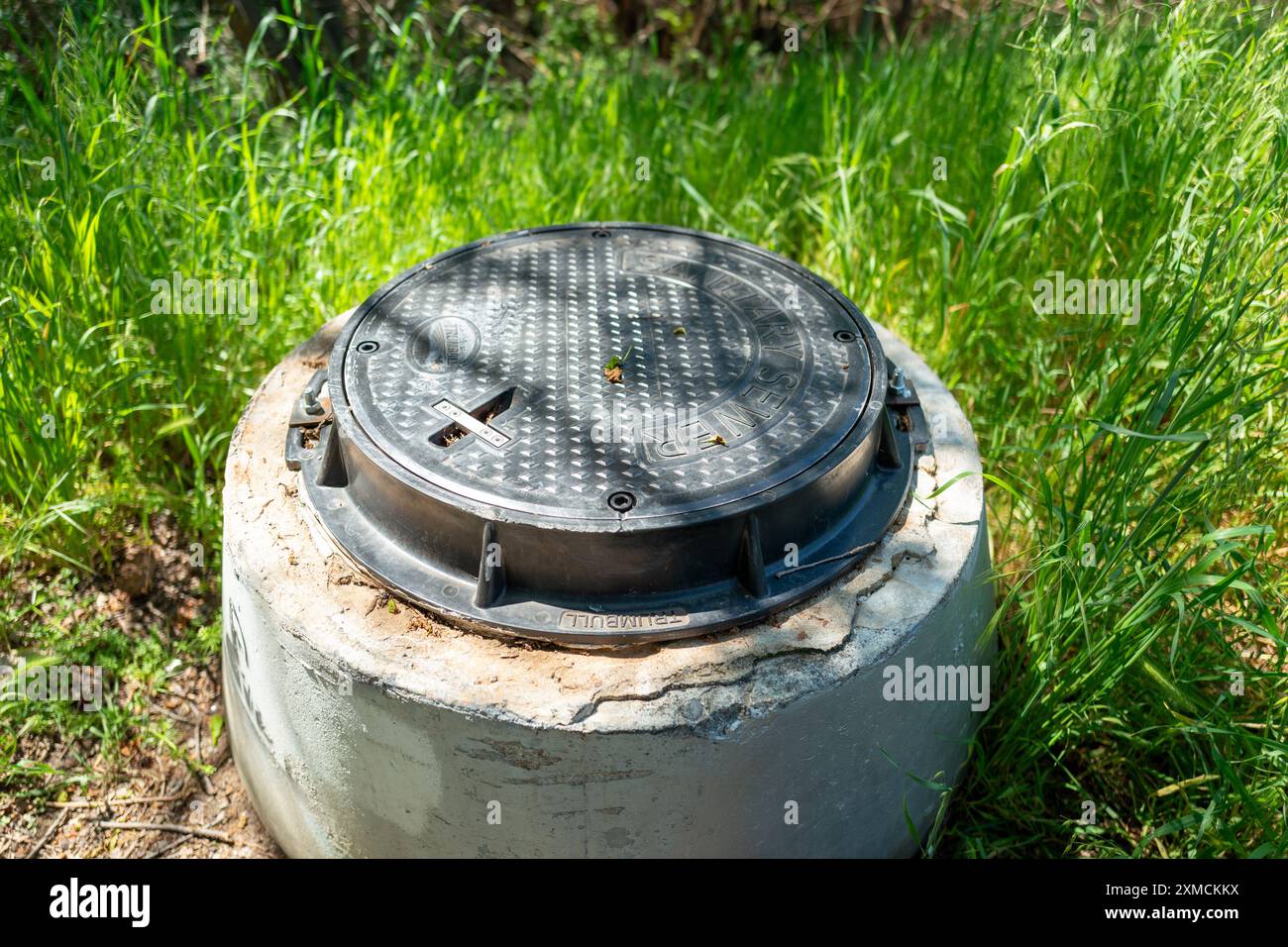 The manhole cover for a sewer is elevated on a concrete pedestal to ...
