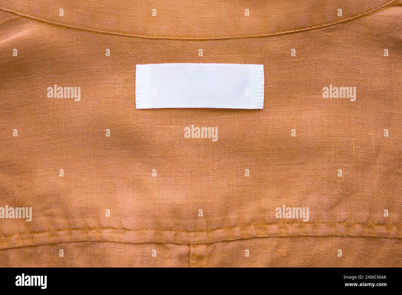 White blank clothing tag label on brown linen shirt fabric texture ...