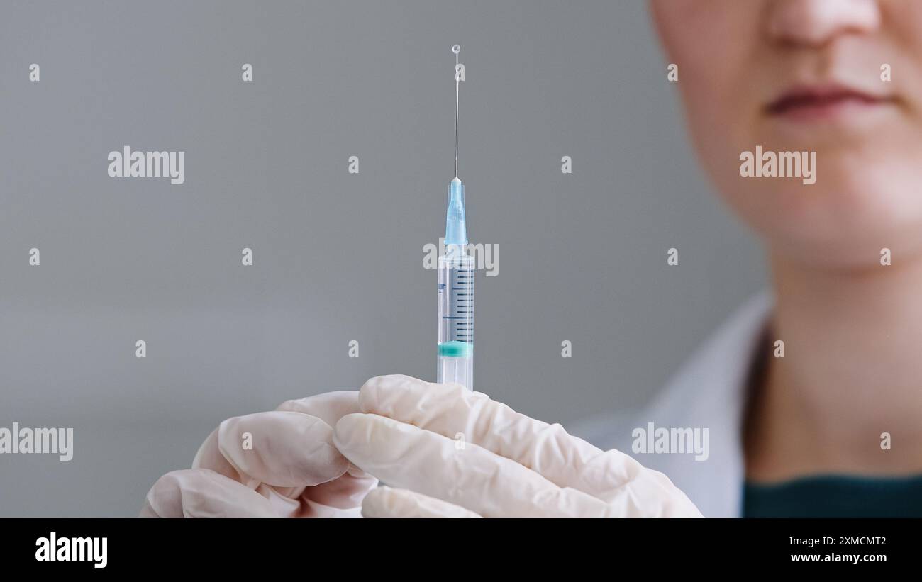 Unrecognizable woman doctor nurse medical worker scientist wears latex gloves holds syringe with ...