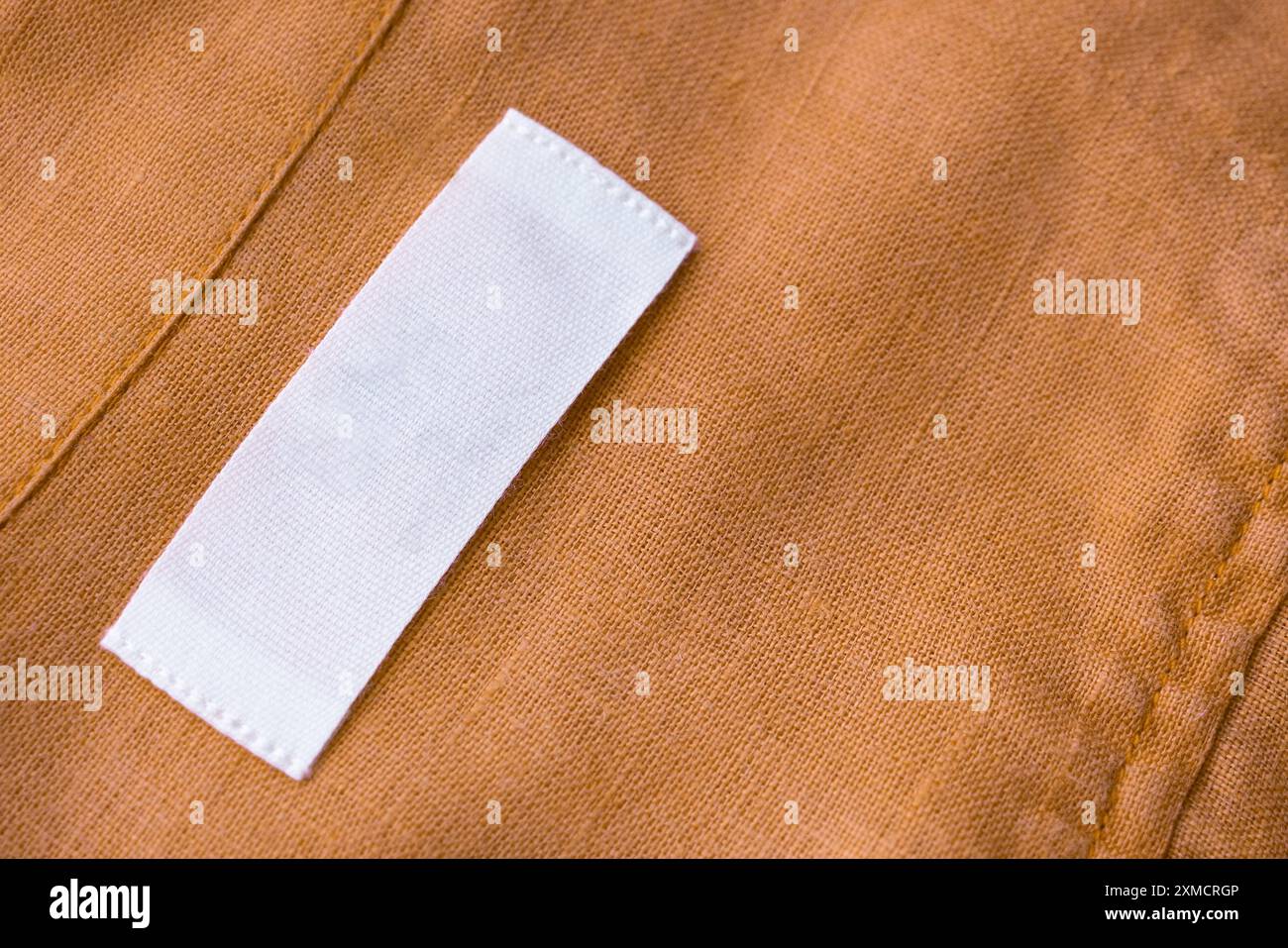 White blank clothing tag label on brown linen shirt fabric texture ...