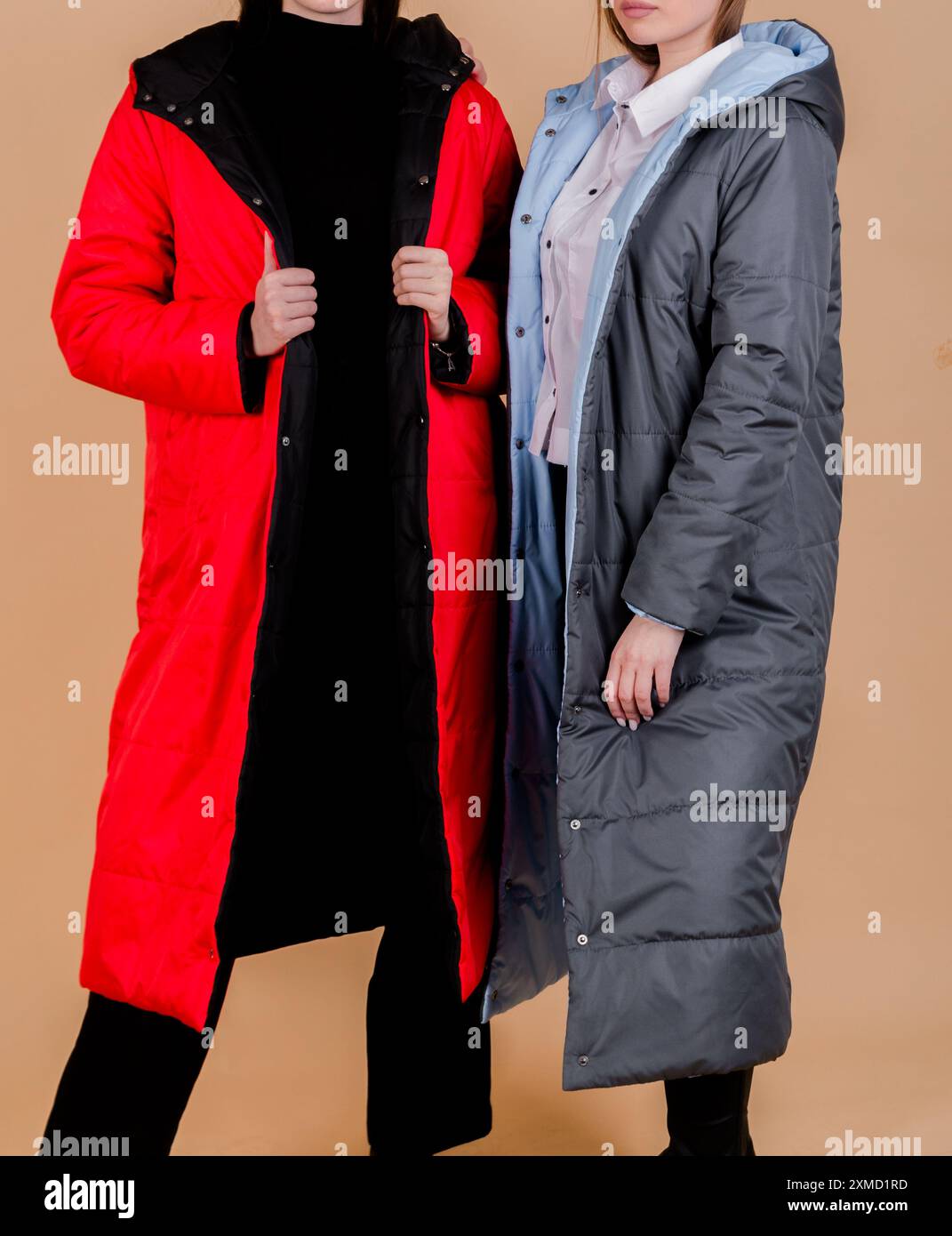 Two women wearing long red and gray coats, standing against a beige ...