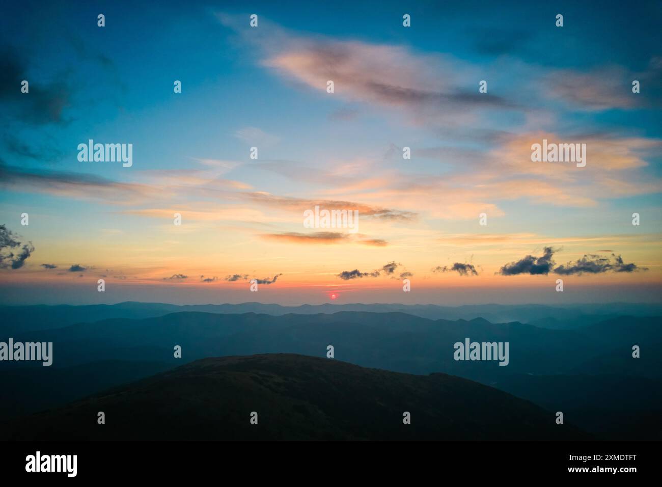 Sun sets behind rolling hills, casting warm, golden glow across sky ...