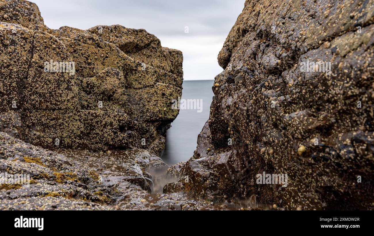 North sea water rushing between two large rocks covered in barnacles ...