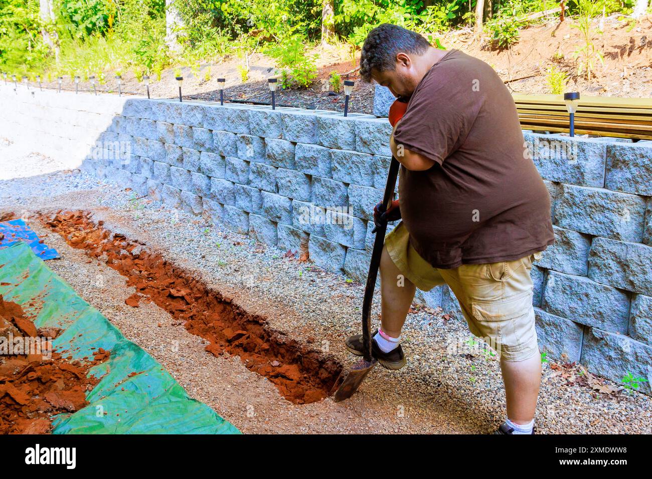 On construction site, worker digs trench to lay perforated pipe as part ...