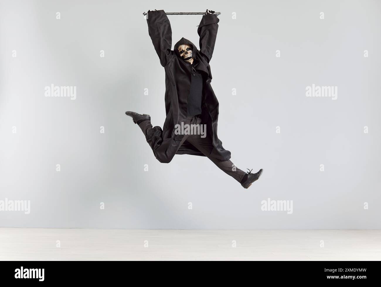 Man in grim reaper death costume jumping with scythe in his hands and ...