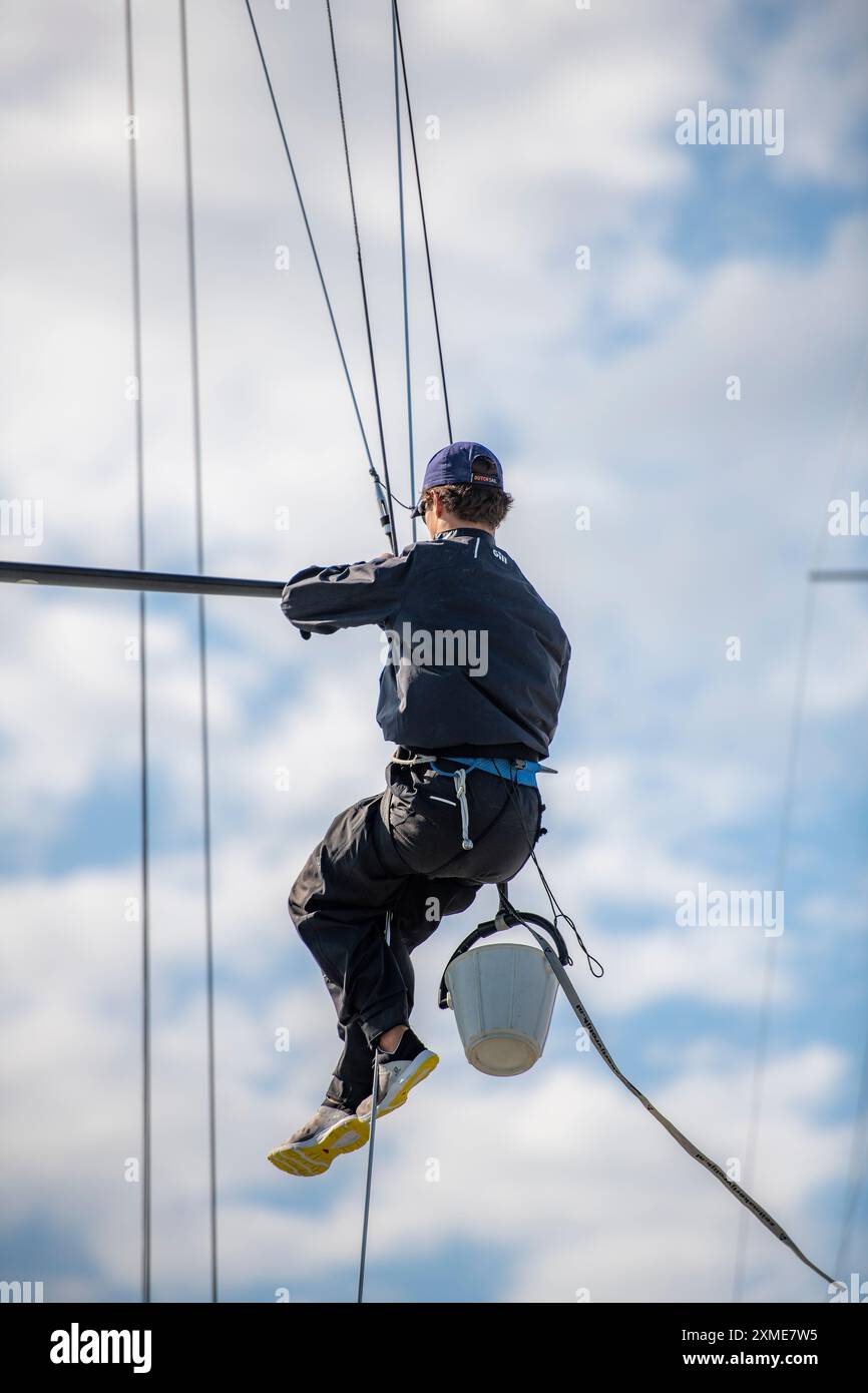 crew member on racing yacht in bosuns chair aloft fixing rigging and ...
