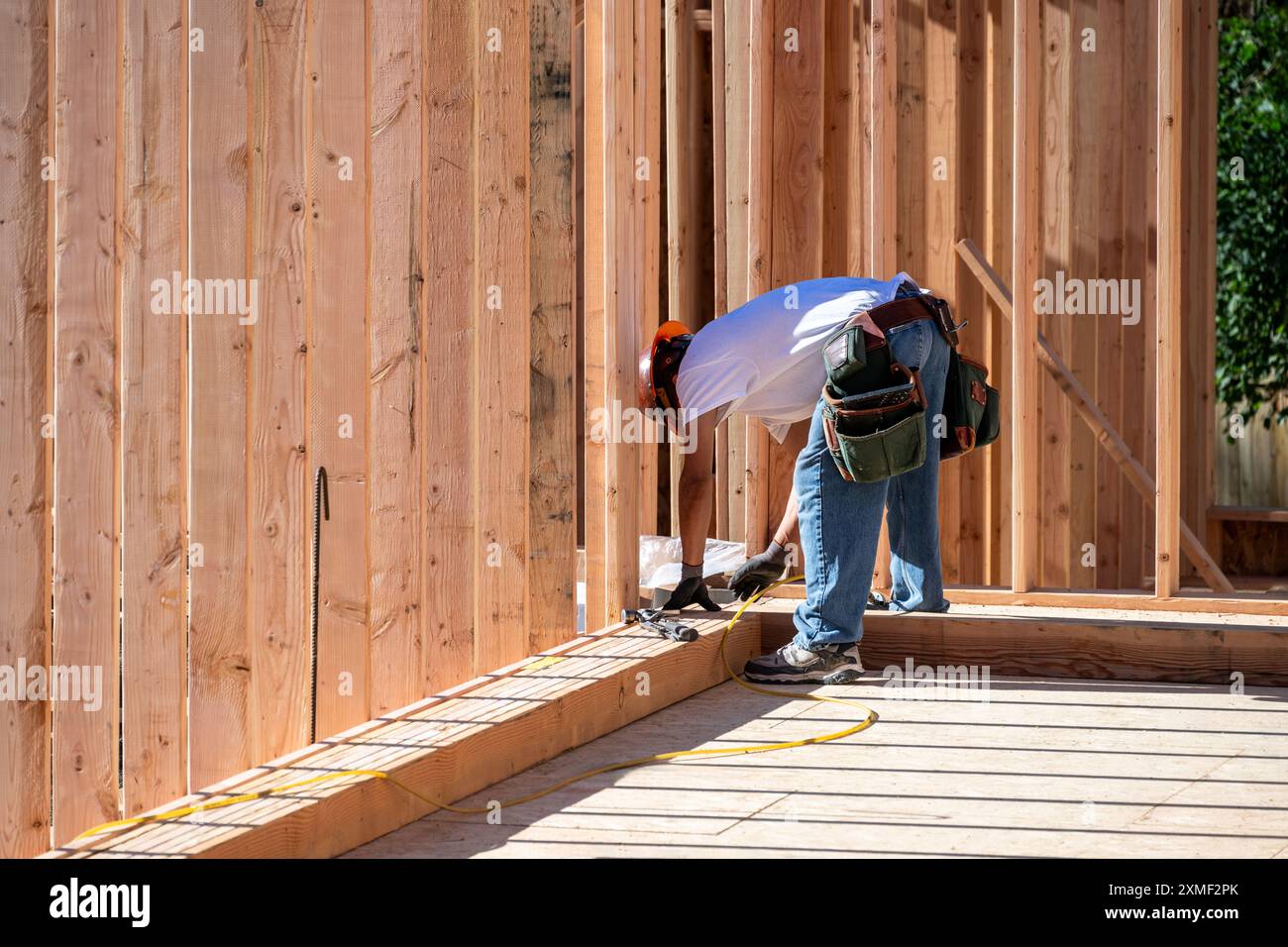 Construction worker in toolbelt and hard hat working with a hammer on new house construction ...