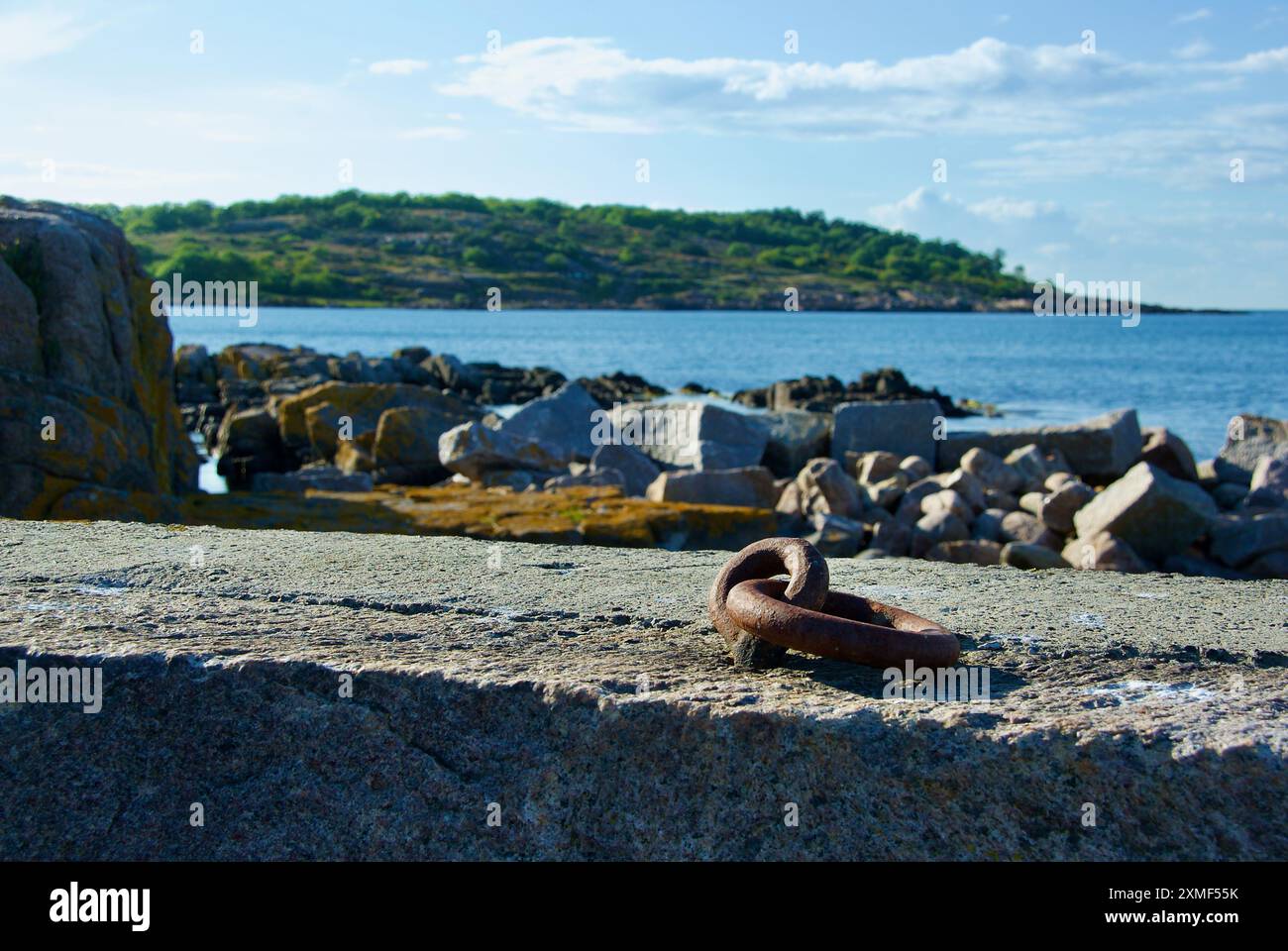 Rusty mooring ring on stone quay with a view over the coastal landscape ...