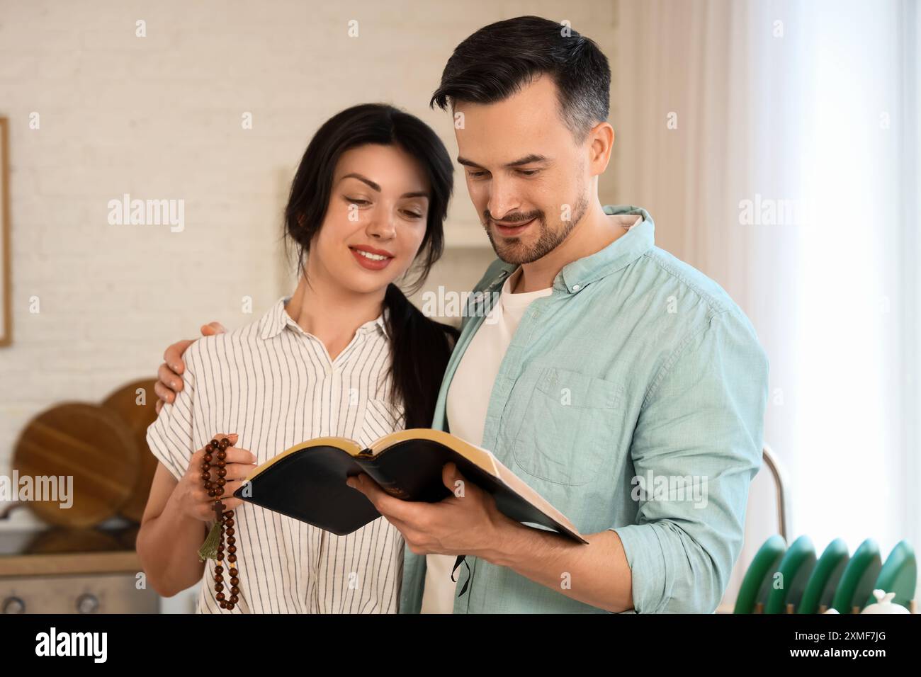 Religious couple with praying beads reading Holy Bible in kitchen Stock ...