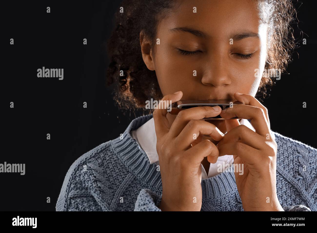 Little African-American girl playing harmonica on dark background ...
