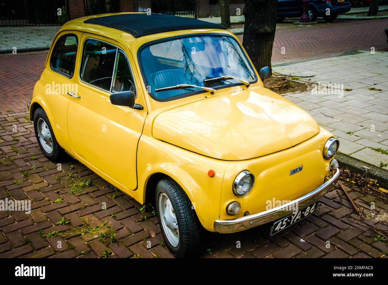 A classic Italian car, the yellow Fiat 500 sits parked on a brick ...
