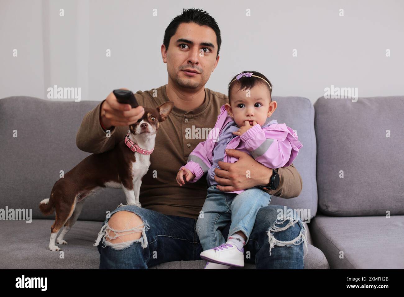 Young dad with baby in arms grabs tv remote control Stock Photo - Alamy