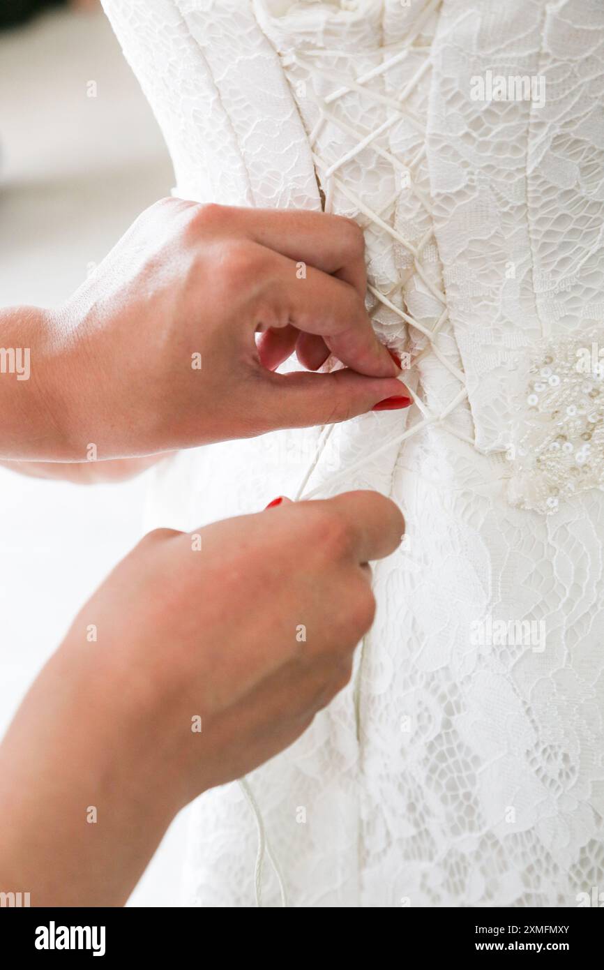 Vertical photo of bridesmaid's hands tying wedding dress laces on back ...