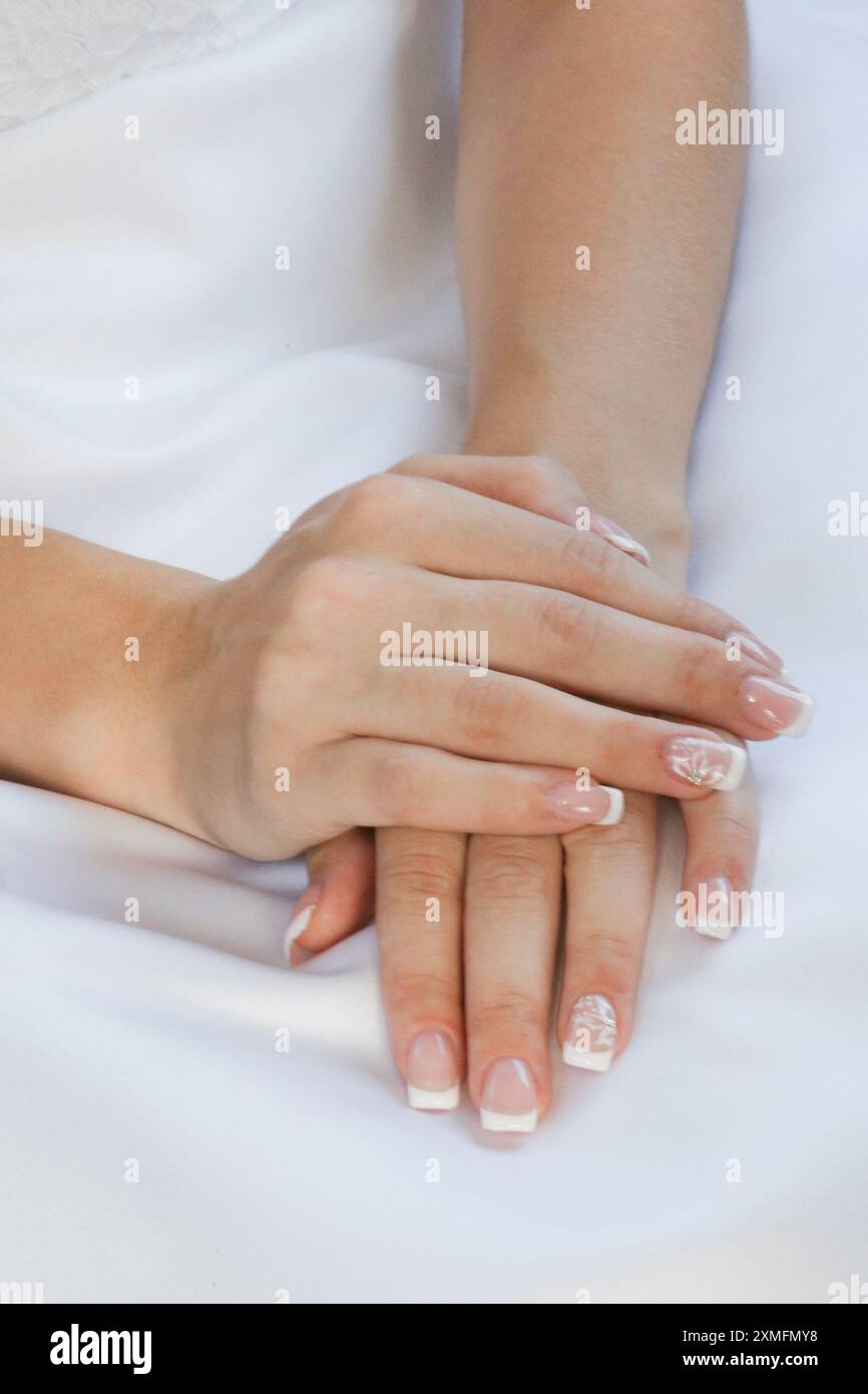 Beautiful young hands lying on a light colored wedding dress, hand on ...