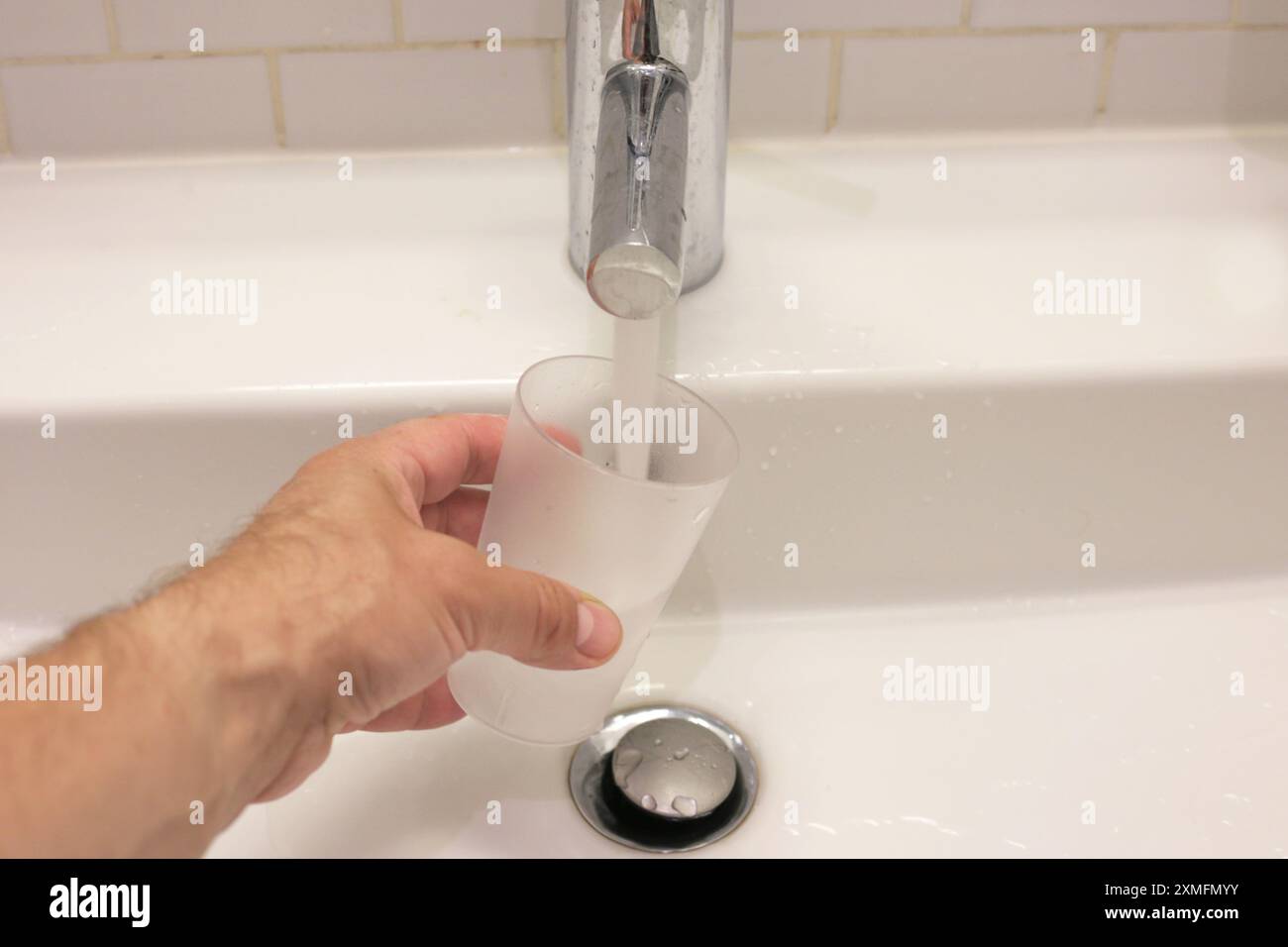 A man's hand pours water from a tap. Water flows from the tap into a ...