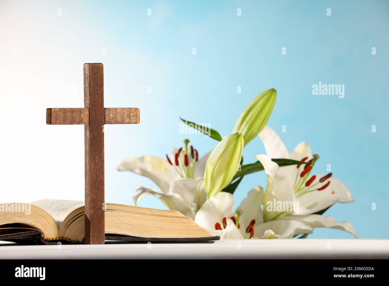Wooden cross, Bible and beautiful lily flowers on white table against ...