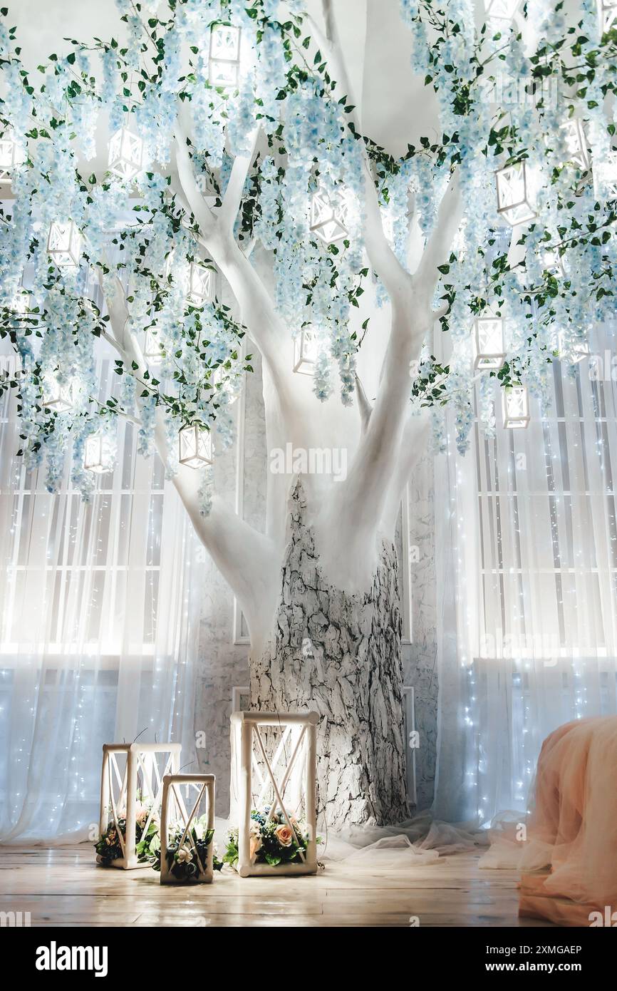 Illuminated white tree with blue flowers and hanging lanterns in a ...