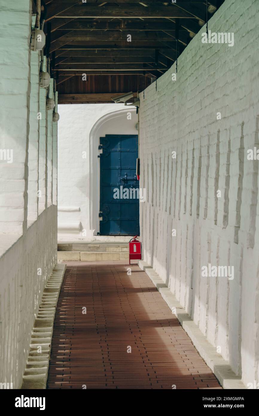 A narrow historic corridor with white walls, arched doorways, and a ...