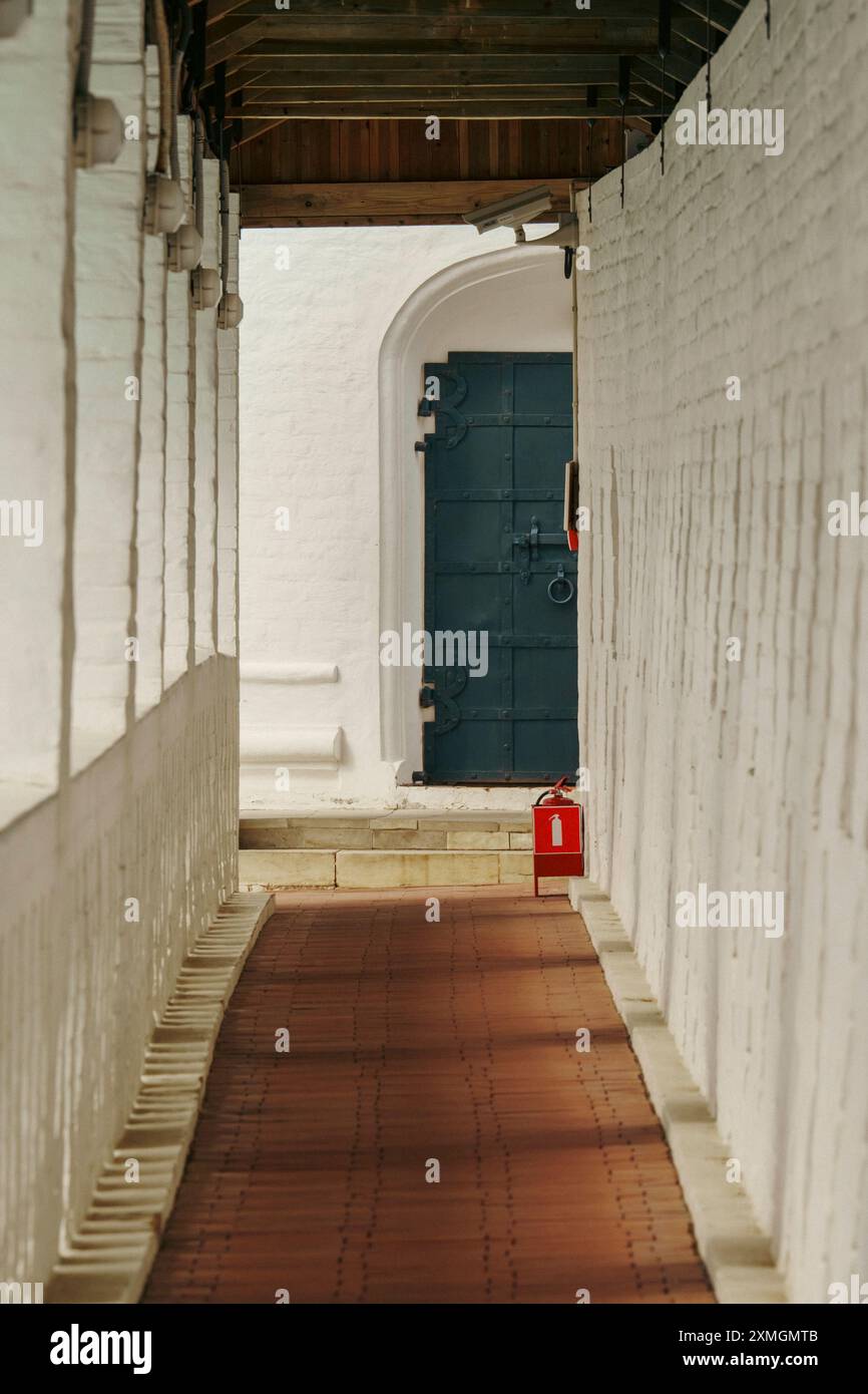 A narrow historic corridor with white walls, arched doorways, and a ...