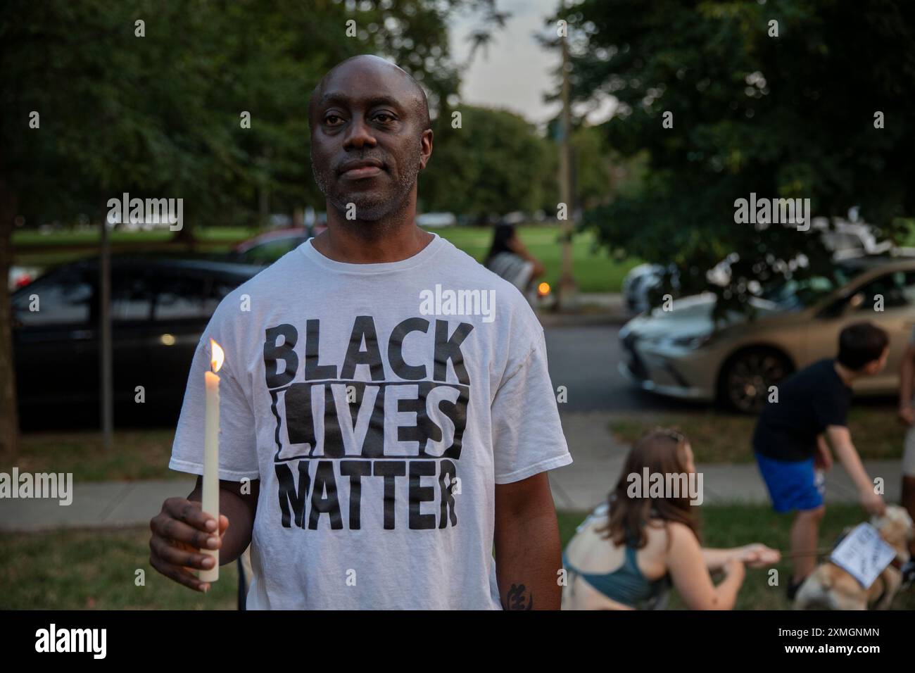 A mourner is holding a candle and wearing a shirt with the text "Black ...