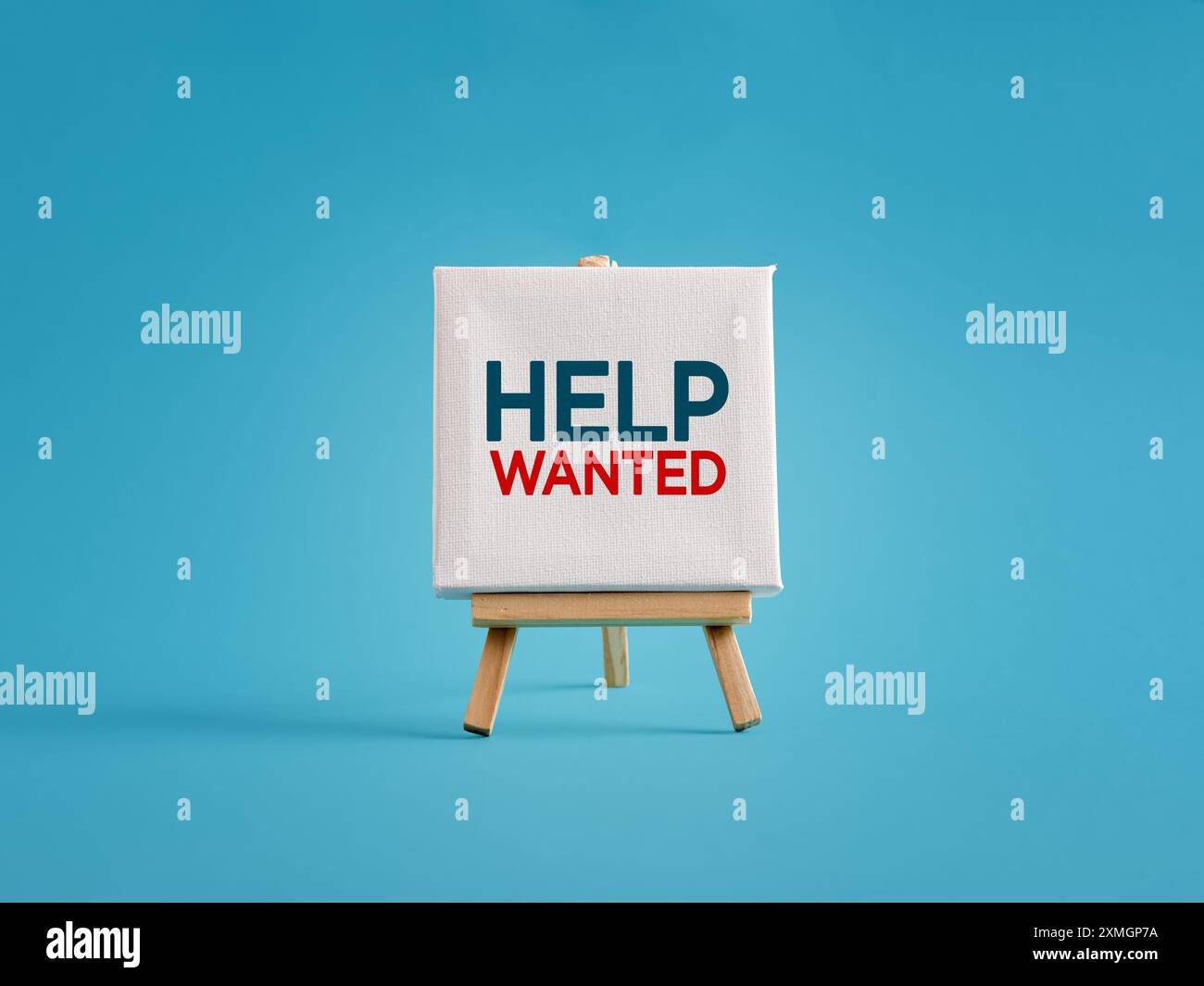 Small wooden easel with help wanted sign displaying on blue background ...