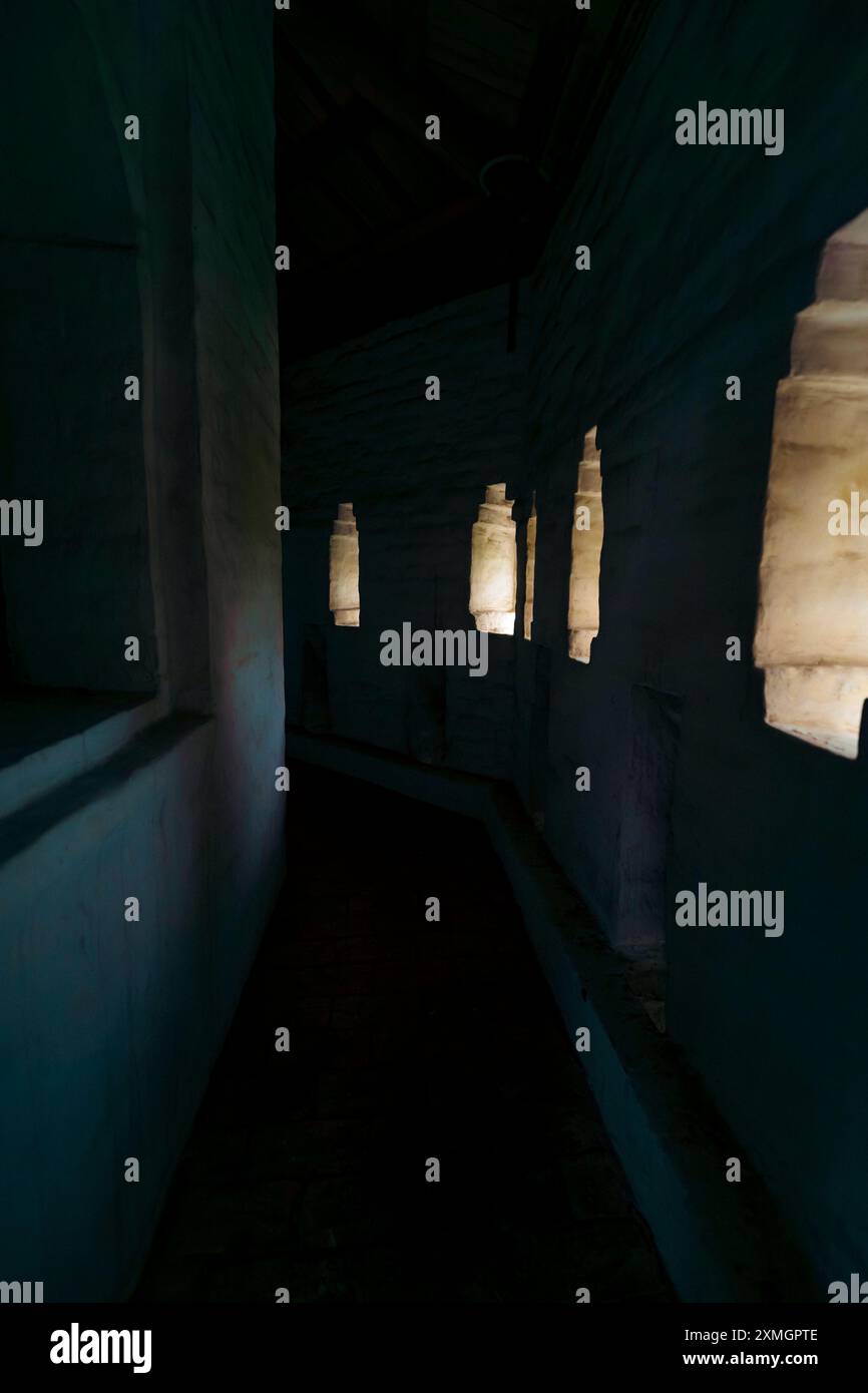 A narrow corridor in a historical building, dimly lit by small windows ...