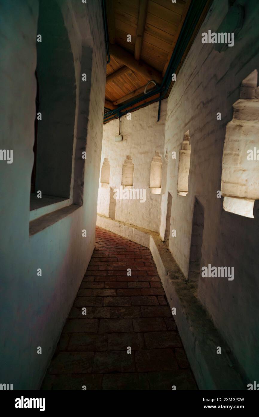 A narrow corridor in a historical building, dimly lit by small windows ...