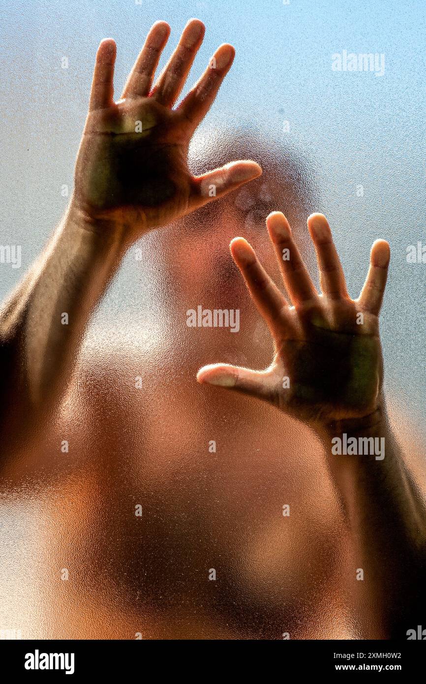 A man is trapped behind a frosted glass panel with his hands pressed against the surface ...