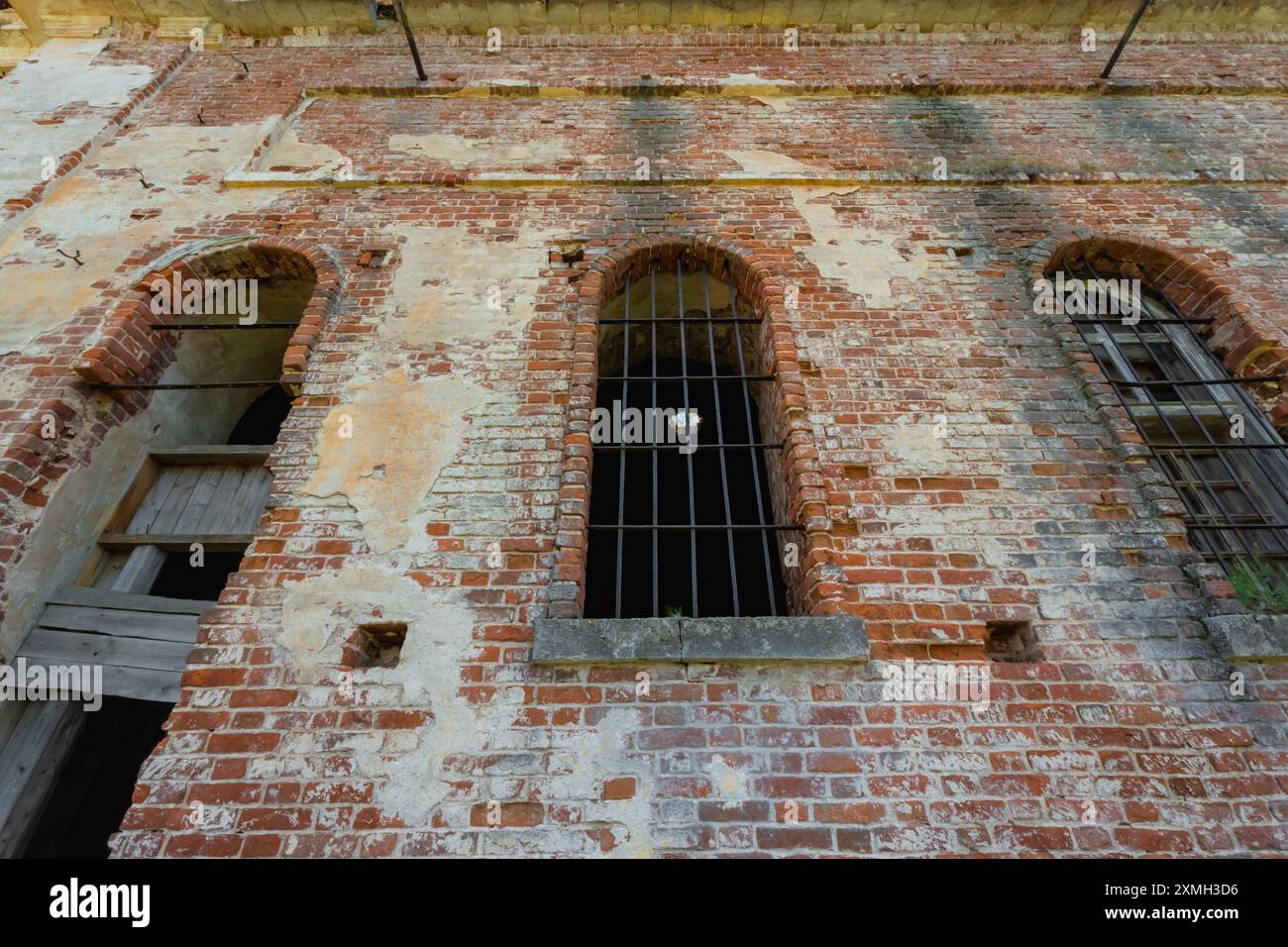 Close-up of an old brick wall featuring three arched windows with iron bars. The wall shows ...