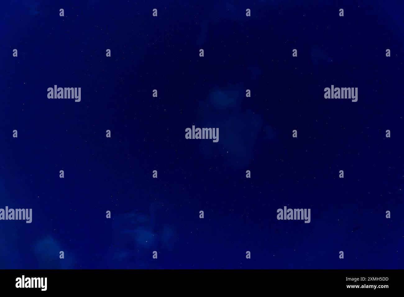 A deep blue night sky filled with numerous stars and faint clouds ...